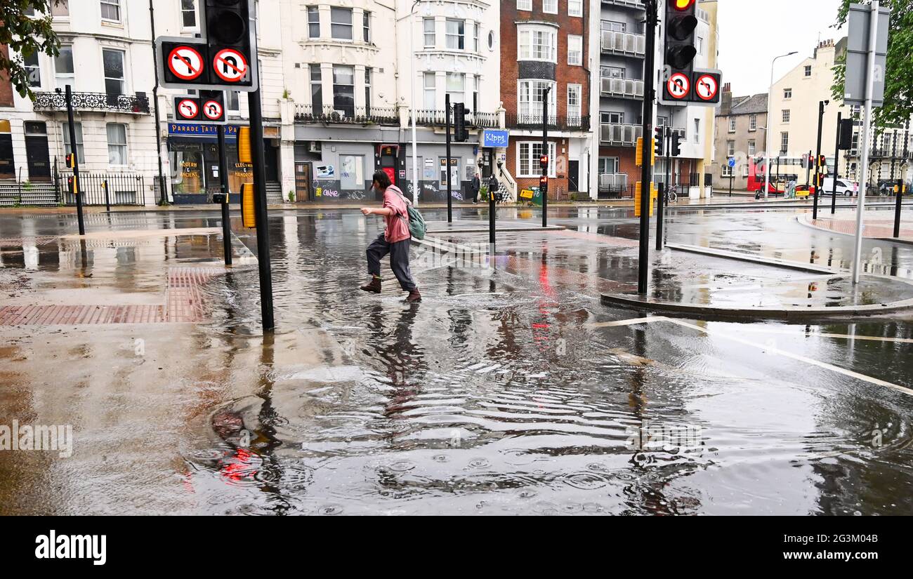 Brighton UK 17th June 2021 - A pedestrian leaps over floodwater on the ...
