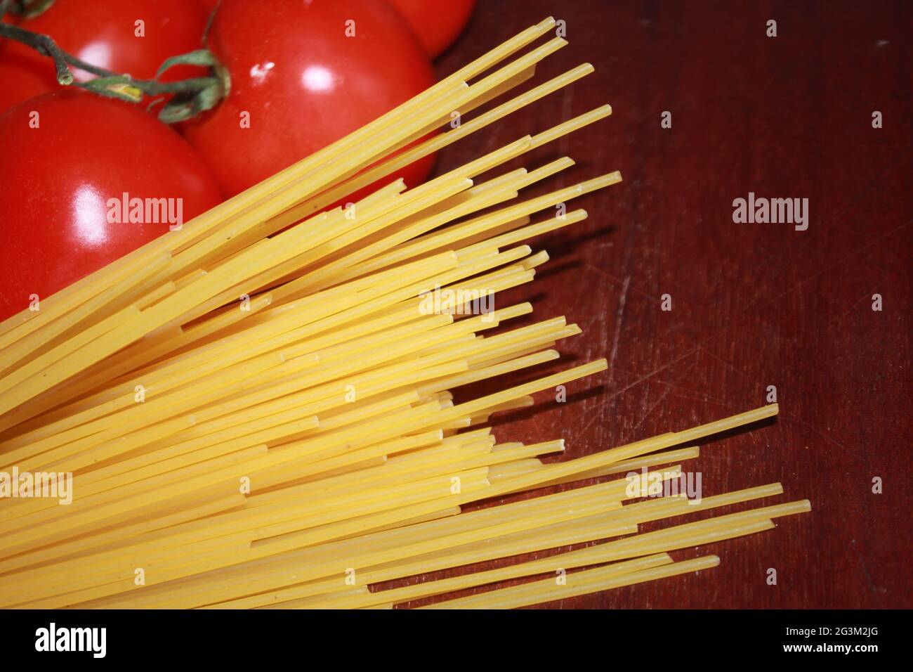 Uncooked spaghetti and tomato closeup photography on a wood background ...