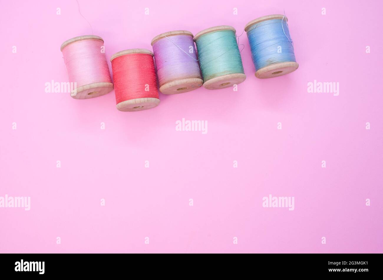 Colorful sewing threads isolated on a pink background with free space ...