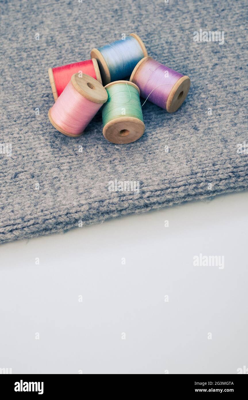 Colorful sewing threads on top of a grey fabric on a white background ...