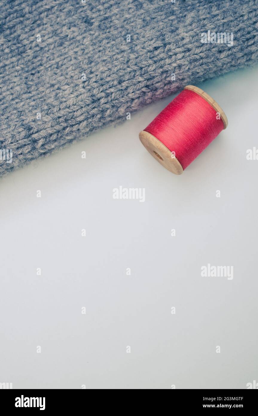 Red sewing thread beside a grey fabric on a white background with free ...