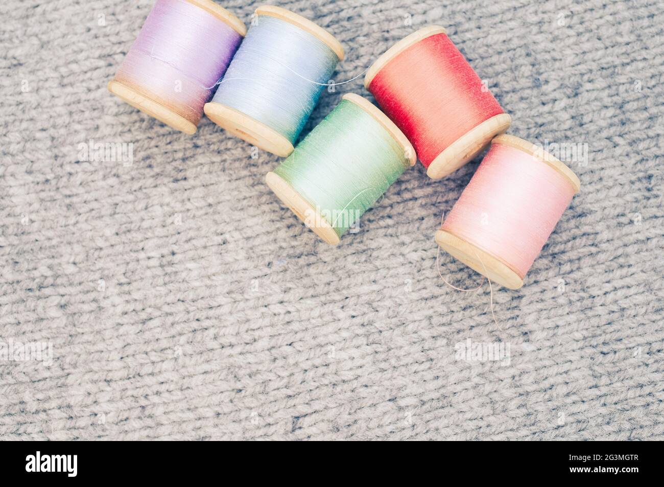 Colorful sewing threads on top of a grey fabric with free space for ...