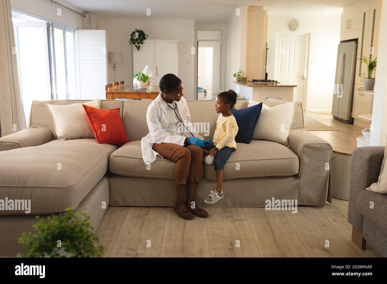 Smiling african american female doctor visiting girl patient at home ...