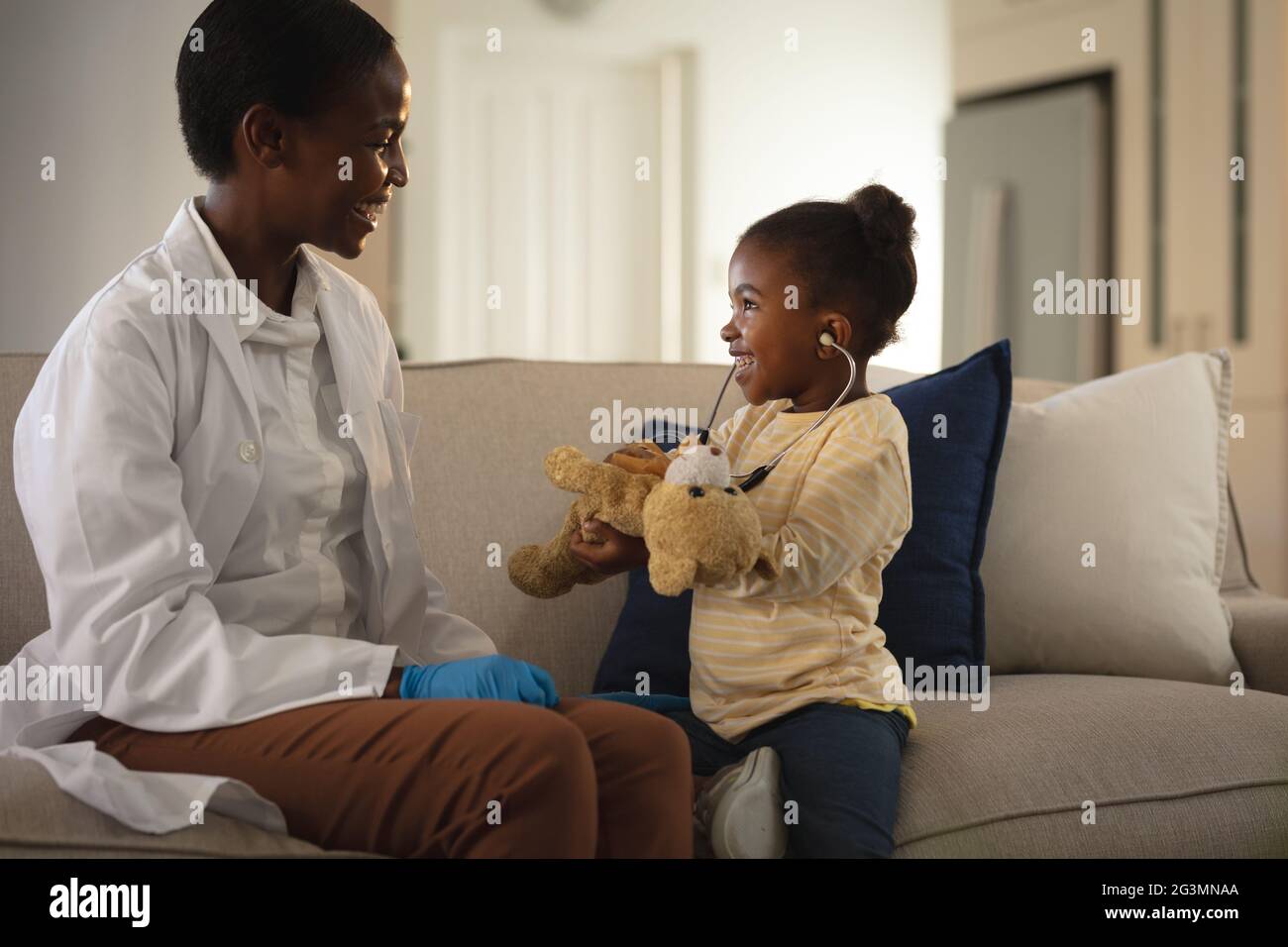 Smiling african american female doctor visiting girl patient at home ...