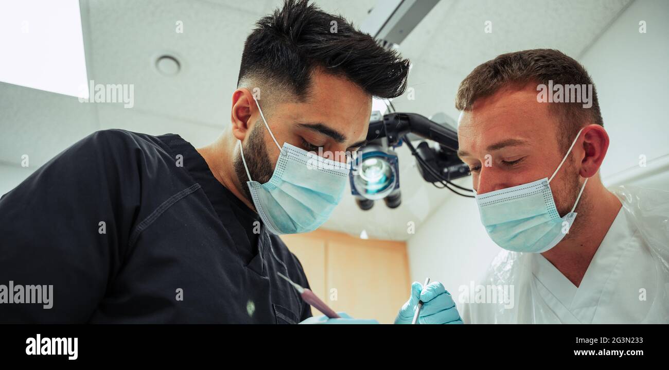 Two male dentists wearing surgical masks operating on patient Stock ...