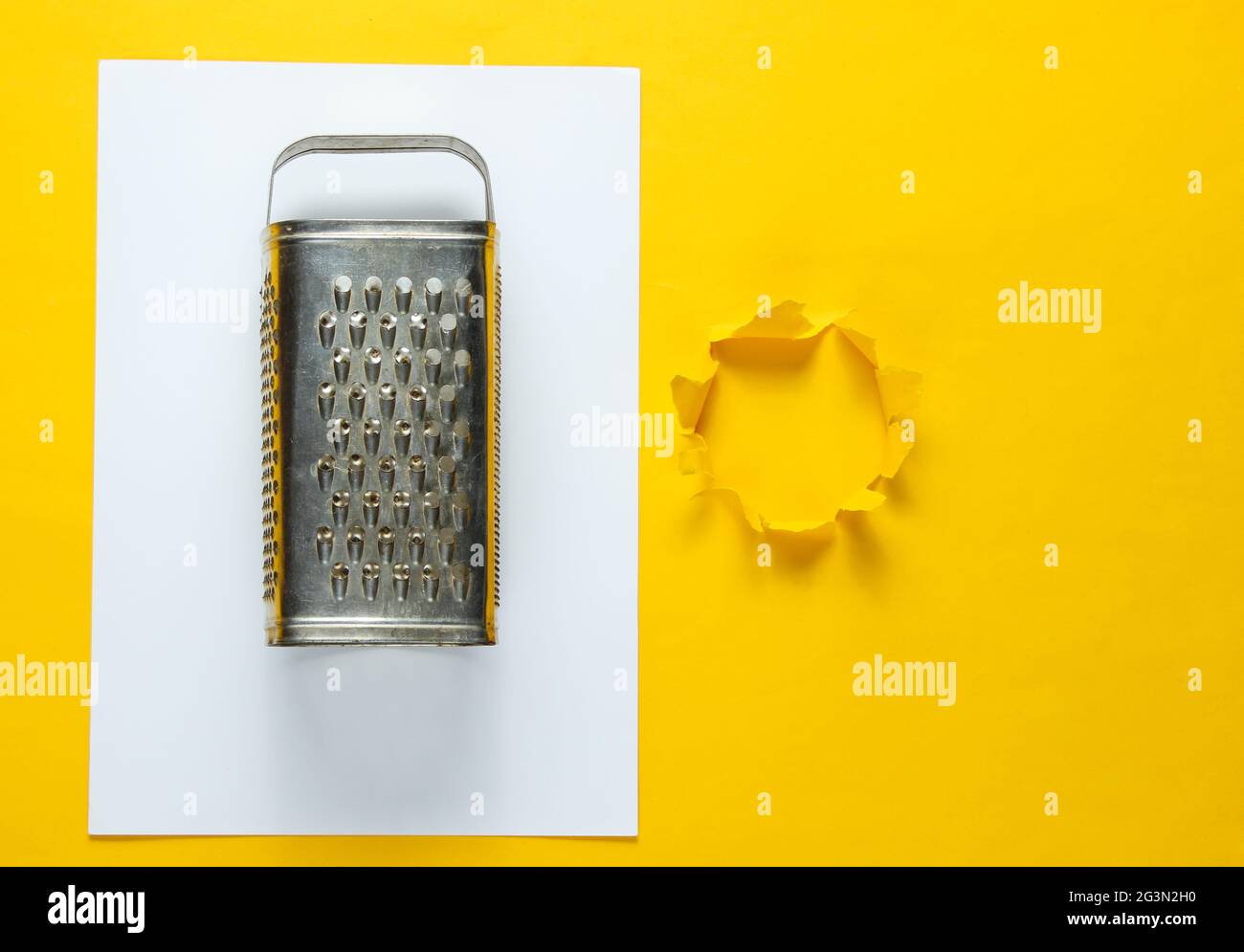 Old metal grater on yellow paper background with torn hole for copy ...