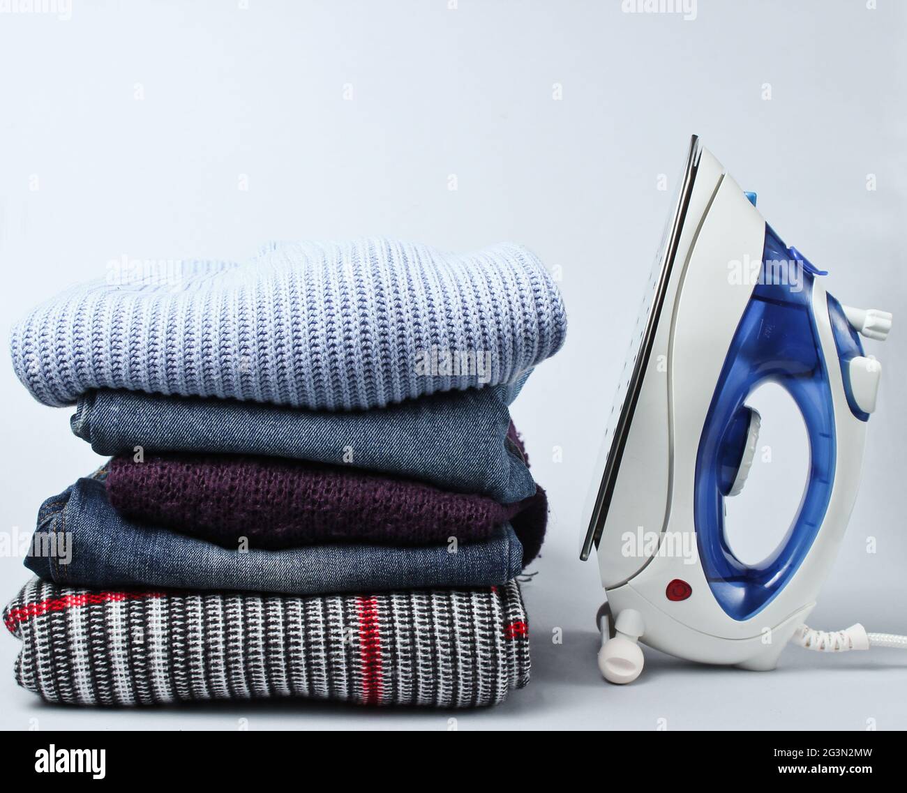Iron and stack of clothes on gray background Stock Photo - Alamy