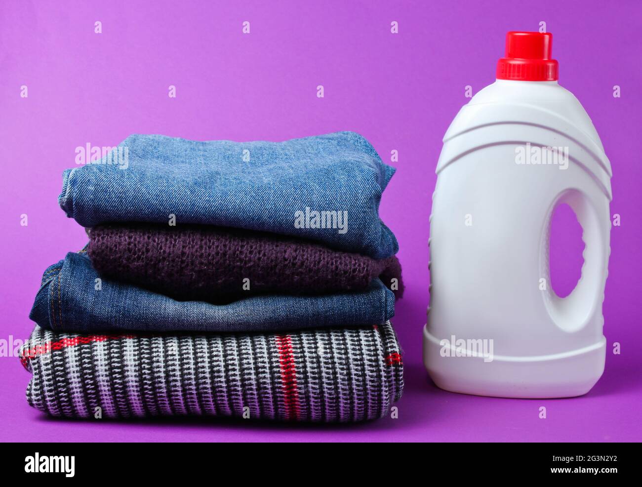 Bottle of washing gel and stack of clothes on purple background Stock ...