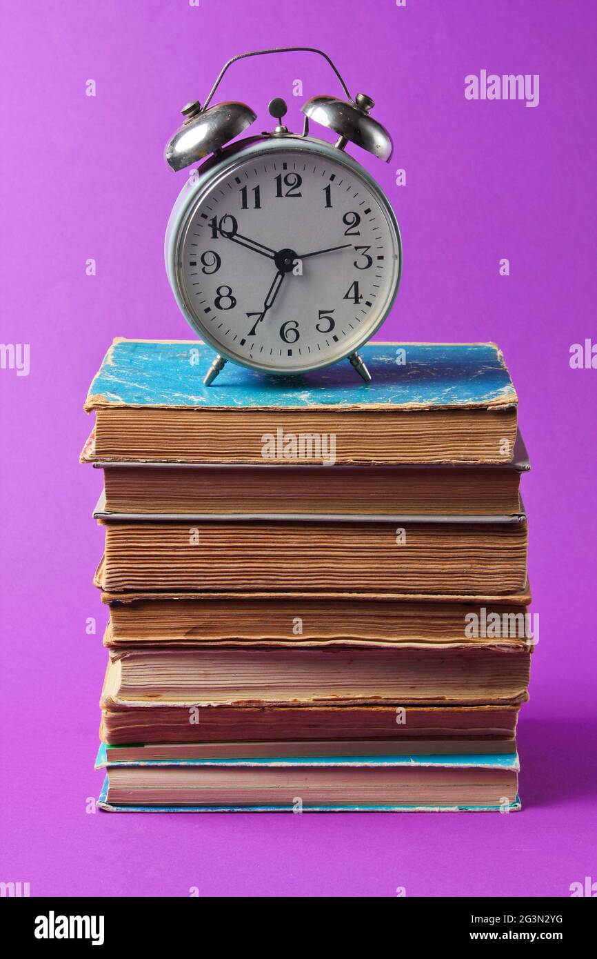 Retro alarm clock on stack of old books on purple background Stock ...
