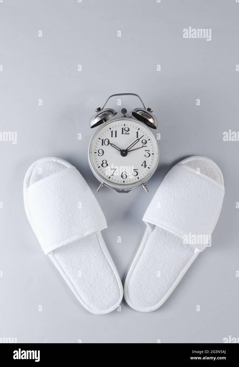 White hotel sleeping slippers and alarm clock on gray background. Time ...