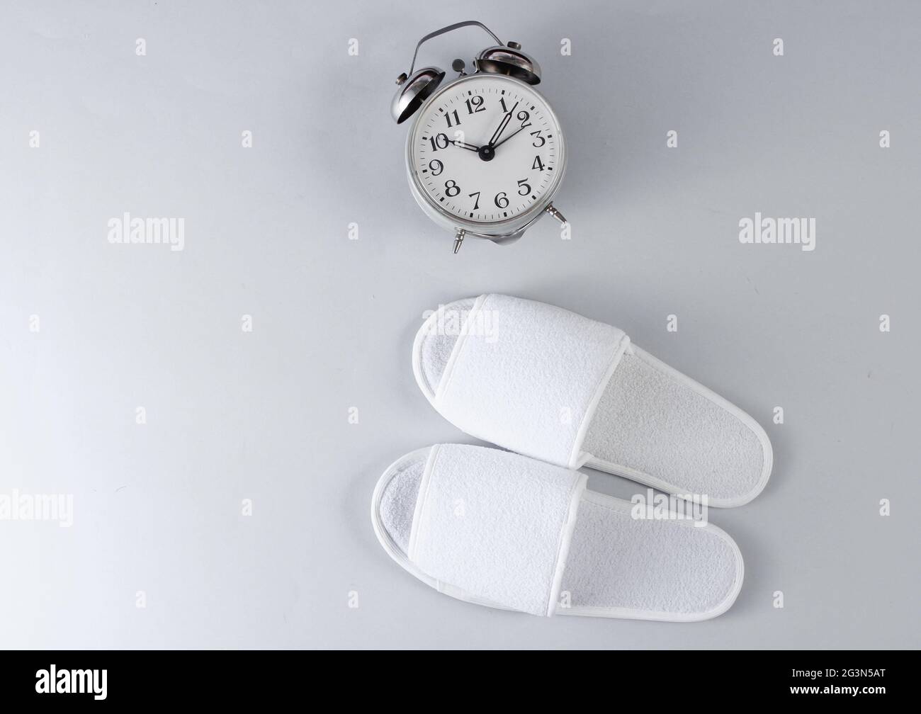White hotel sleeping slippers and alarm clock on gray background. Time ...