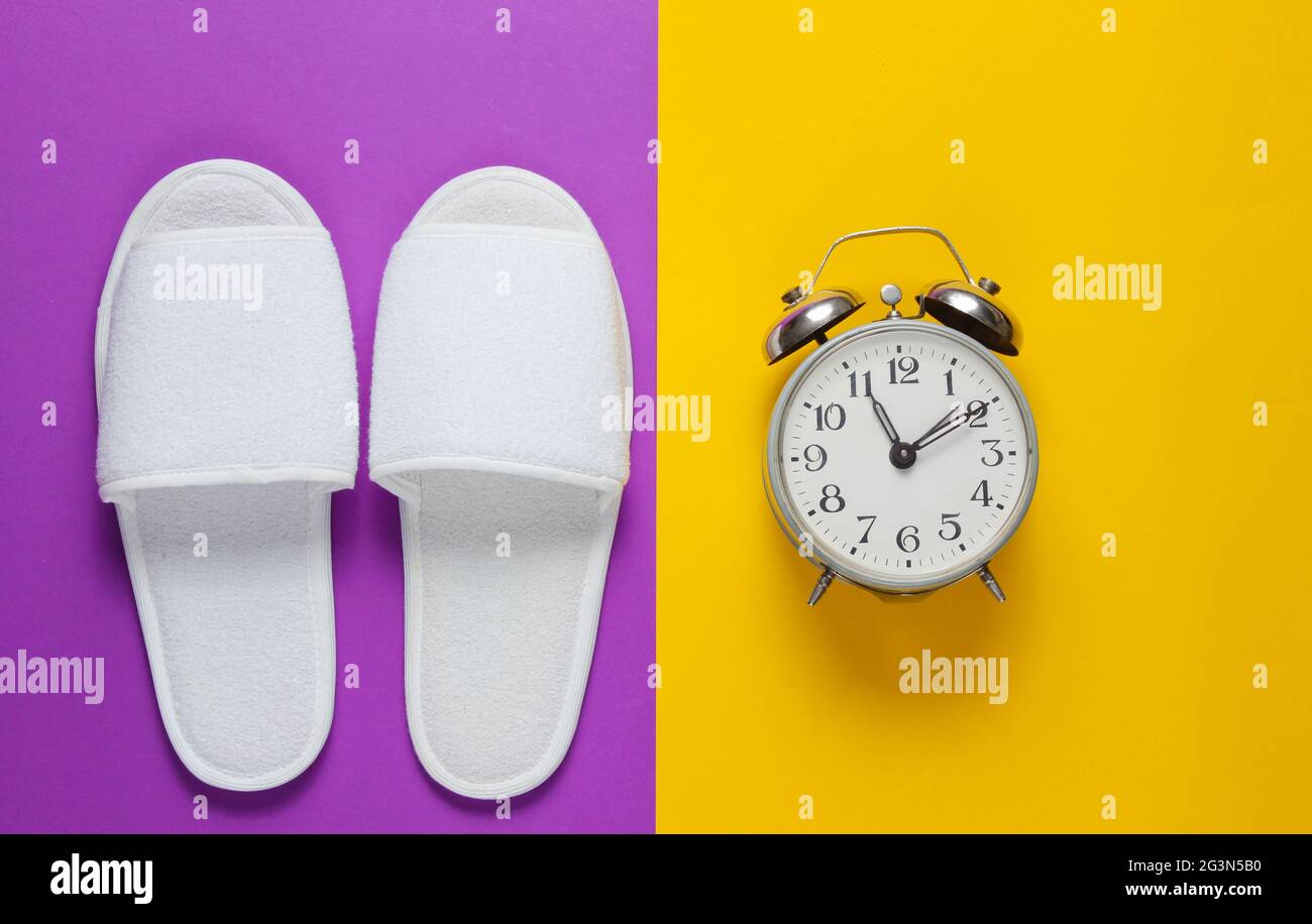White hotel sleeping slippers and alarm clock on colored background ...
