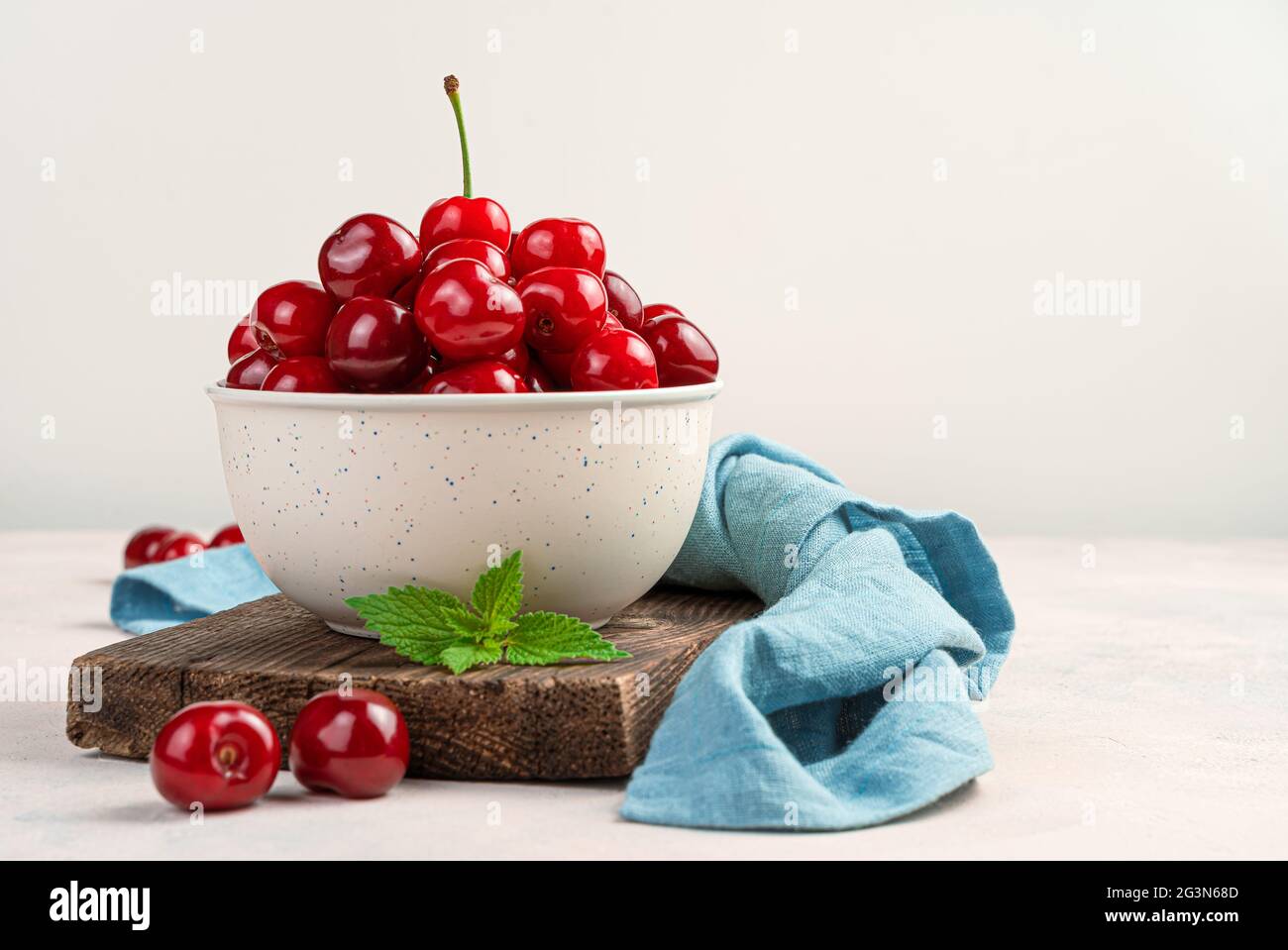 A bowl with ripe juicy cherries on a light background. Side view, copy ...