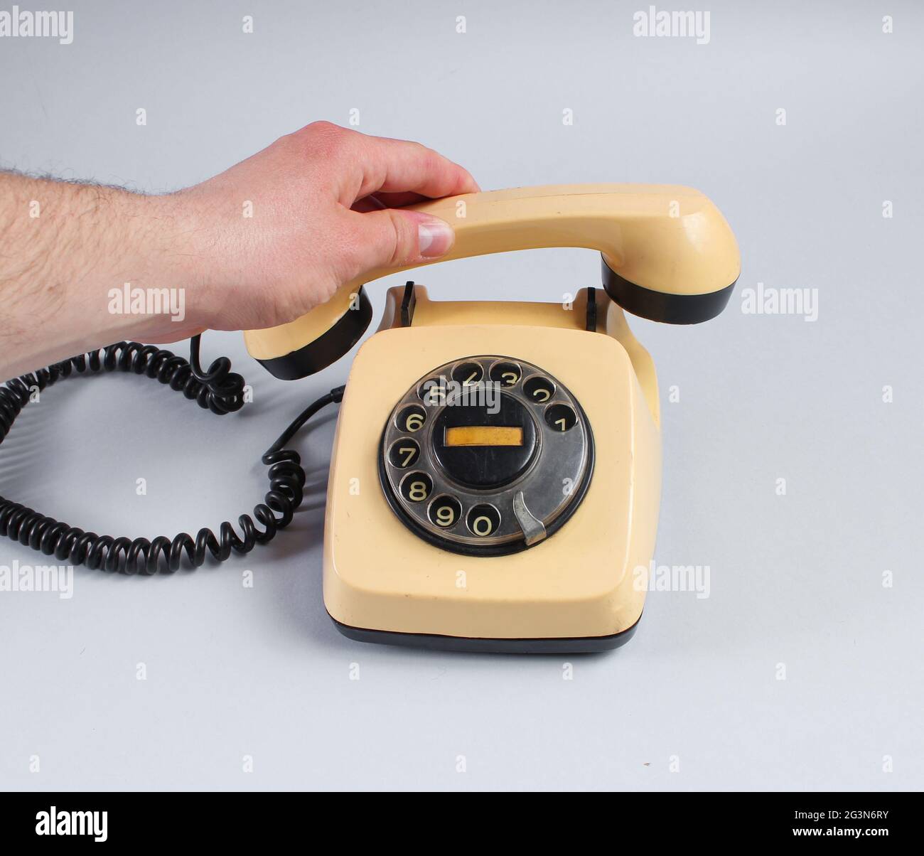 Male hand holding a rotary retro telephone handset on a gray background ...