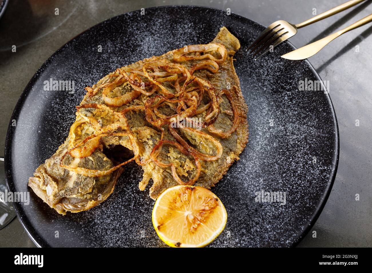 fried flounder with onion and lemon on a black clay plate Stock Photo ...