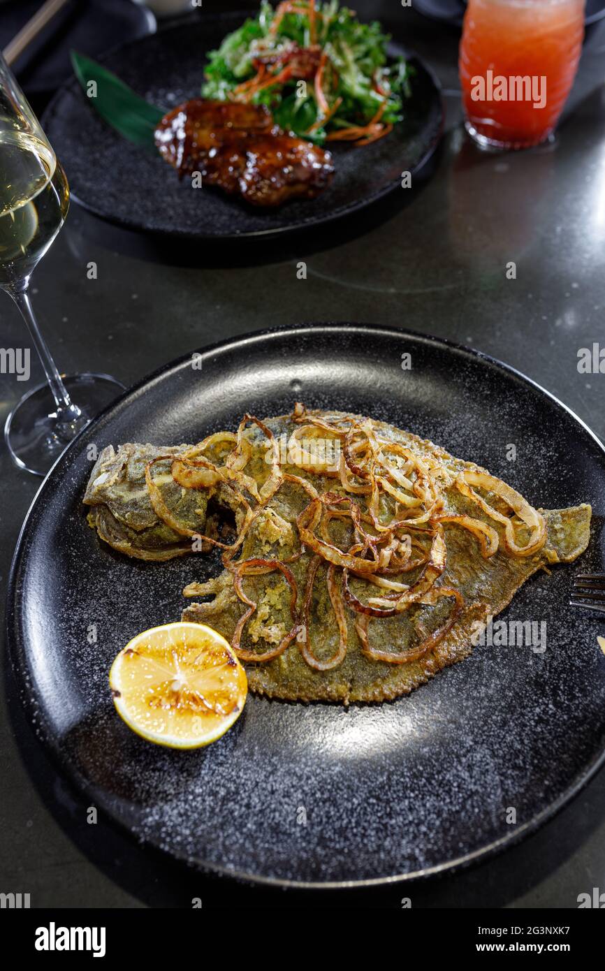 fried flounder with onion and lemon on a black clay plate Stock Photo ...