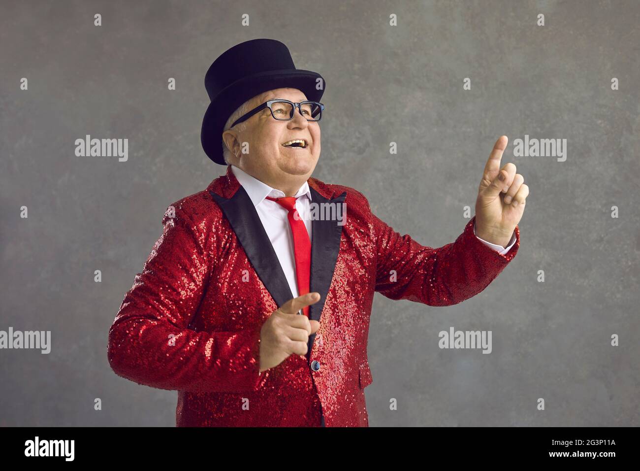 Funny senior man in retro party outfit dancing and having fun on gray ...