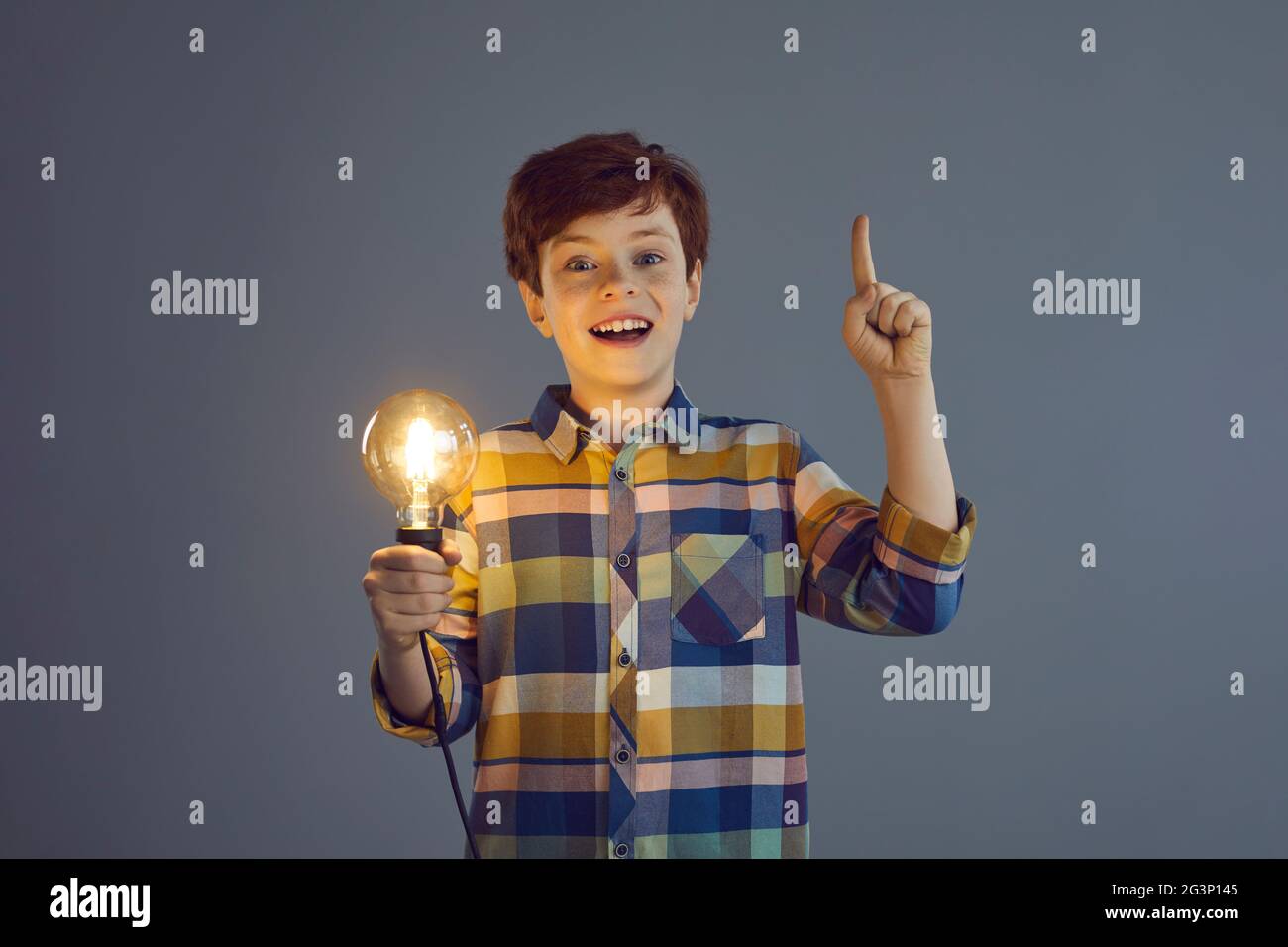 Amazed boy child holding glowing light bulb standing on grey studio ...