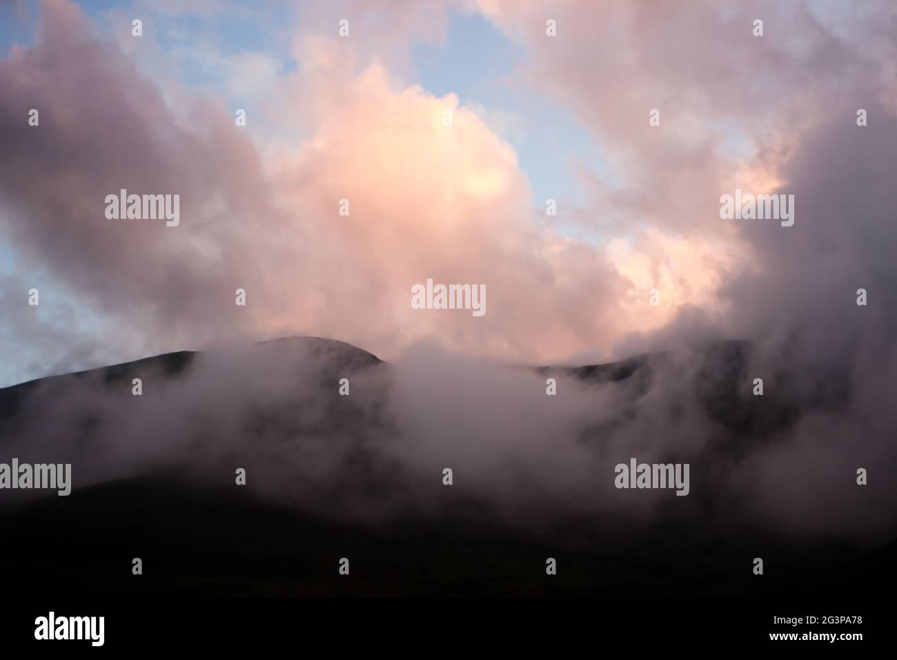 Clouds and fog, colored pinkish by the setting sun, gathering around a ...