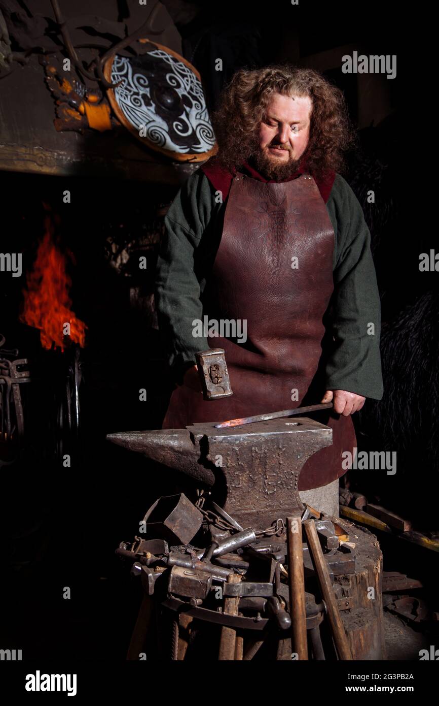 Viking forges weapons and swords in the smithy. A man in a warrior's ...