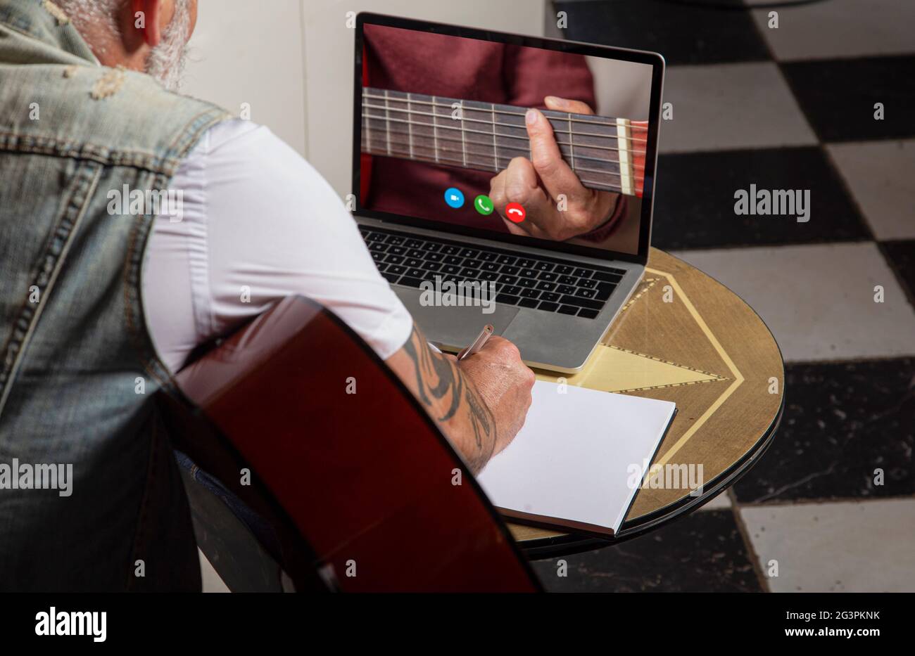 Man jotting down notes in notebook while taking online classes on ...