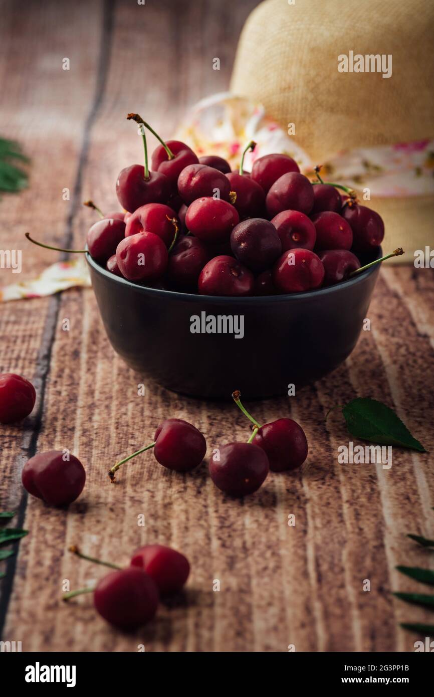Vertical shot of fresh red cherries on a bowl with a hat on a wooden ...