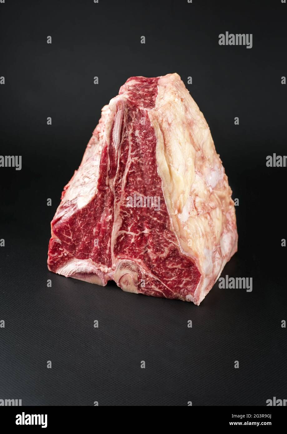 Raw dry aged wagyu porterhouse beef block offered as close-up on black ...