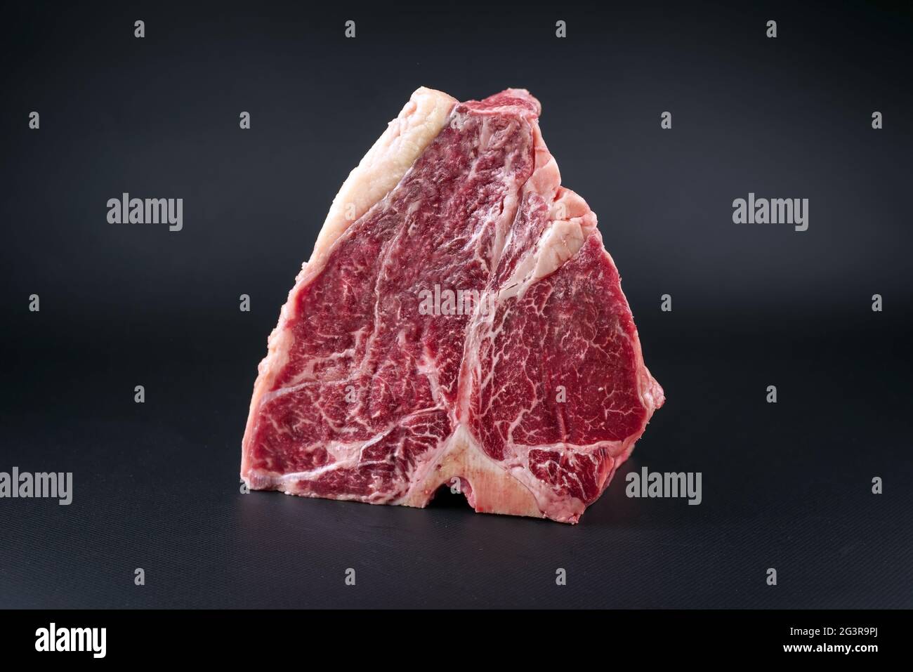 Raw dry aged wagyu porterhouse beef block offered as close-up on black ...