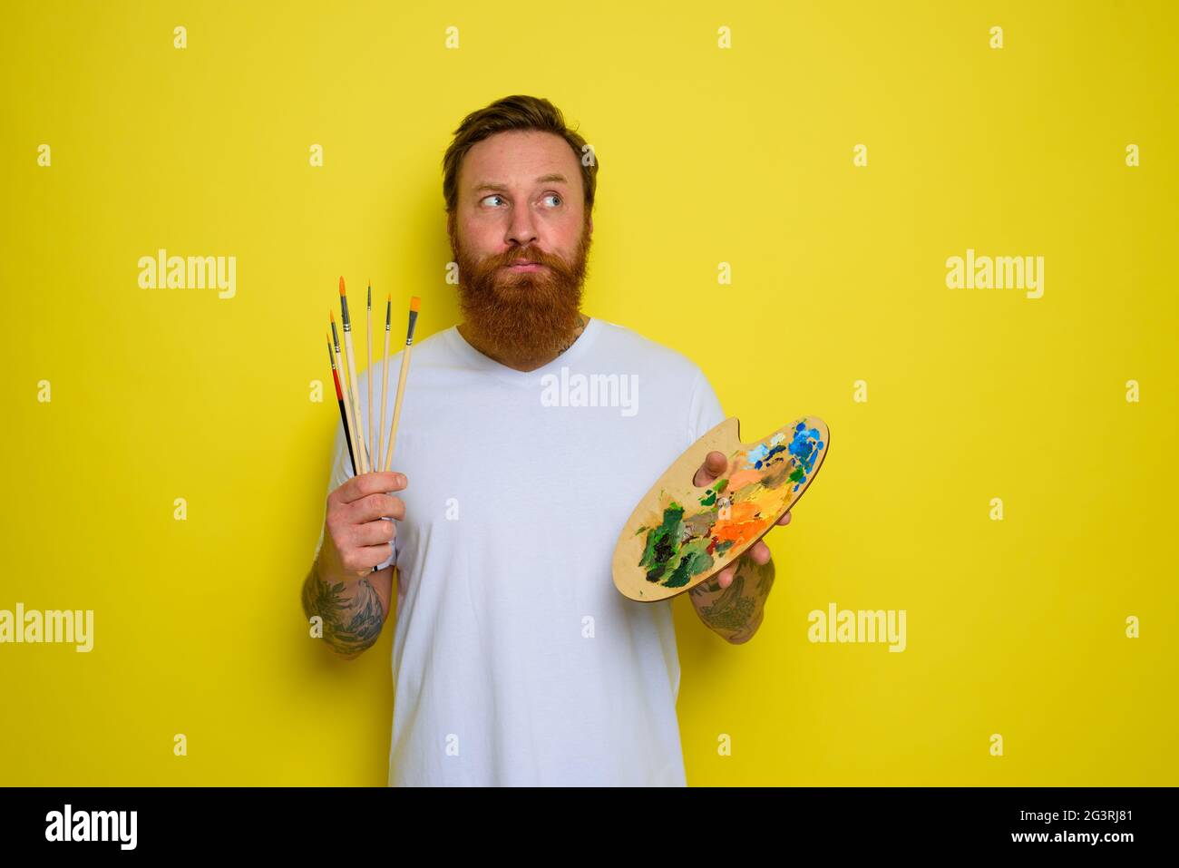 Undecided man with beard and tattoo is ready to draw with brushes Stock ...