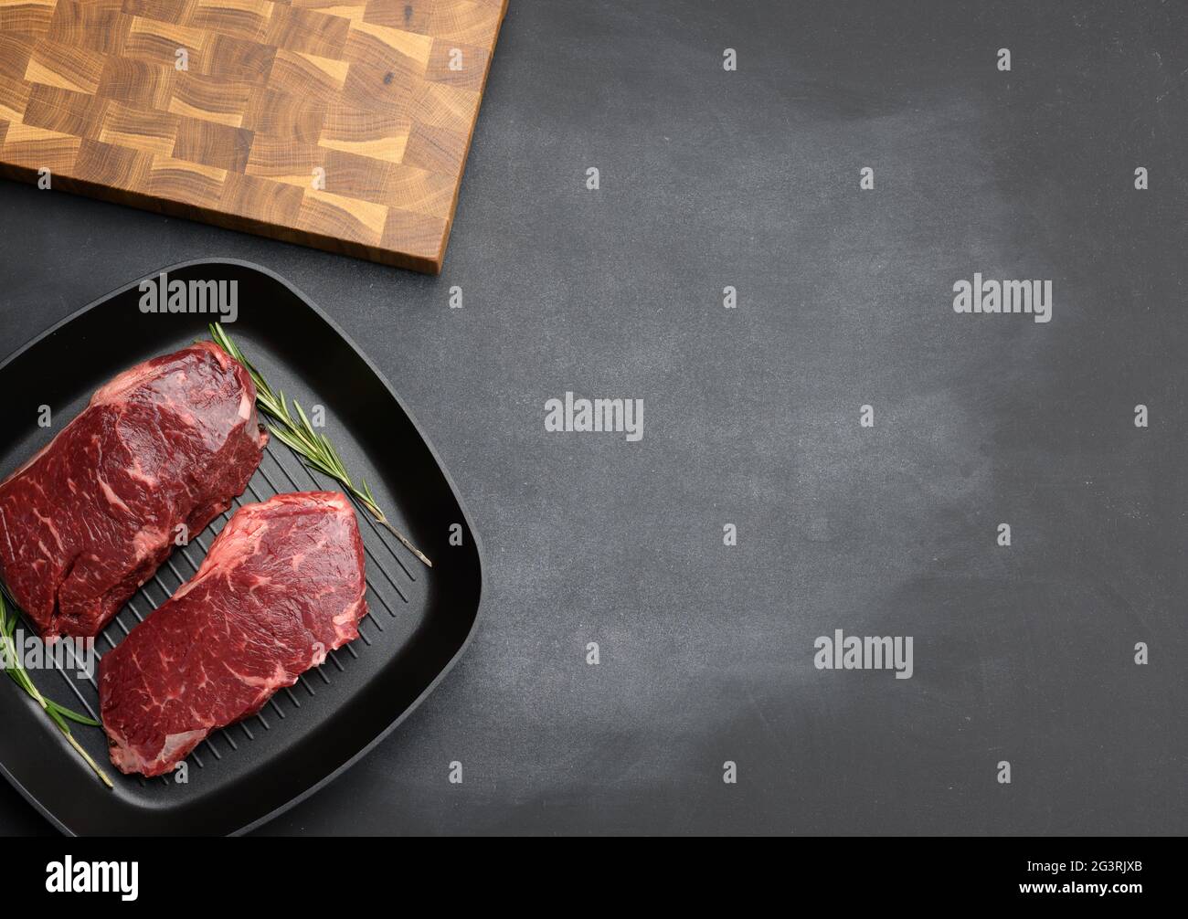 two raw pieces of beef in a black square grill pan, steaks on a black ...