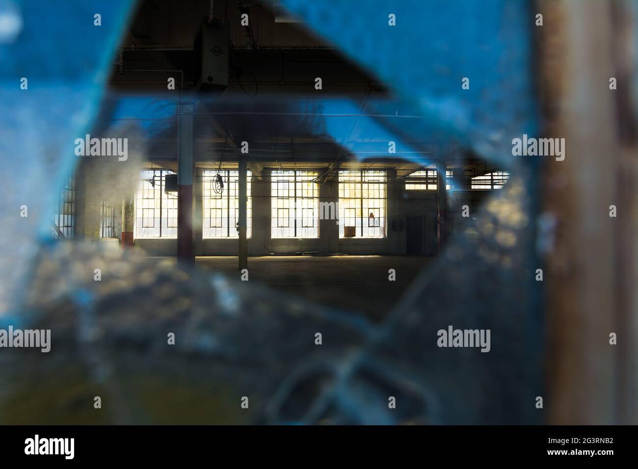 Horizontal photograph inside empty warehouse through broken window pane ...