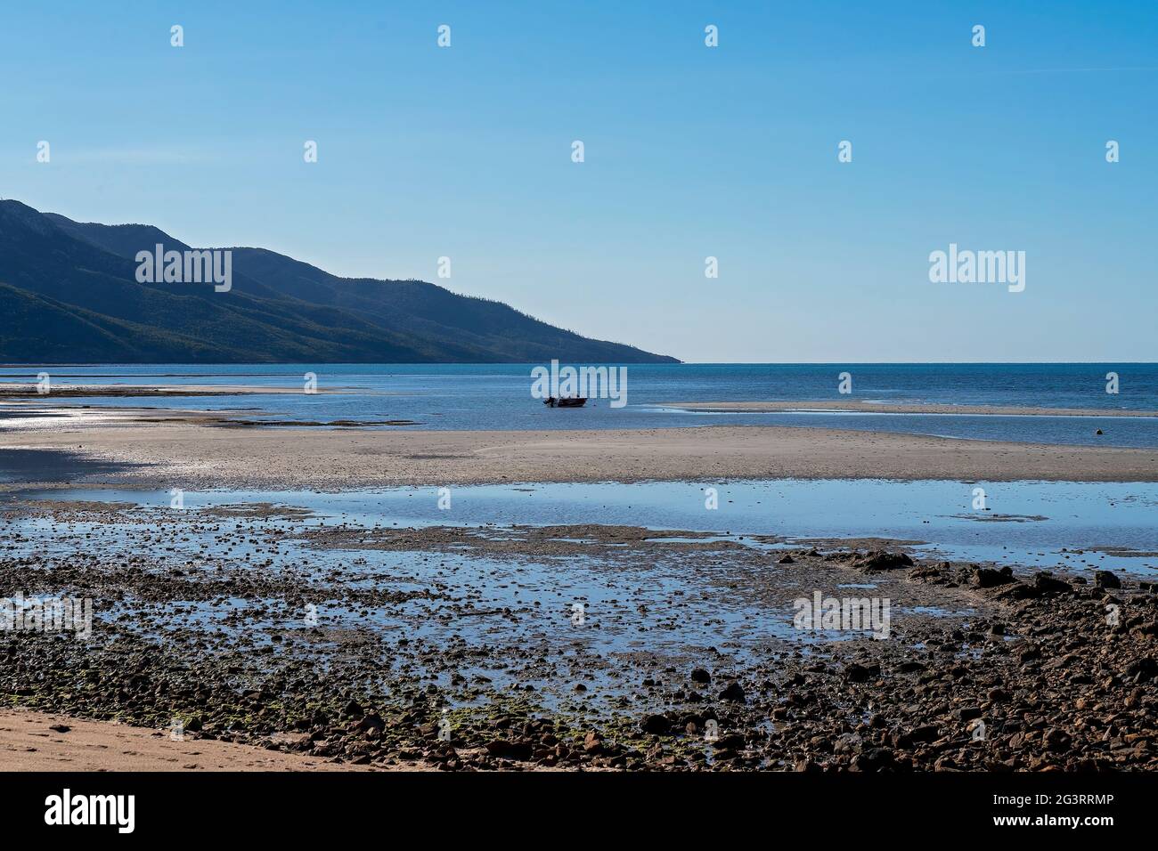Muddy rocky seabed at low tide with small boat anchored offshore Stock ...