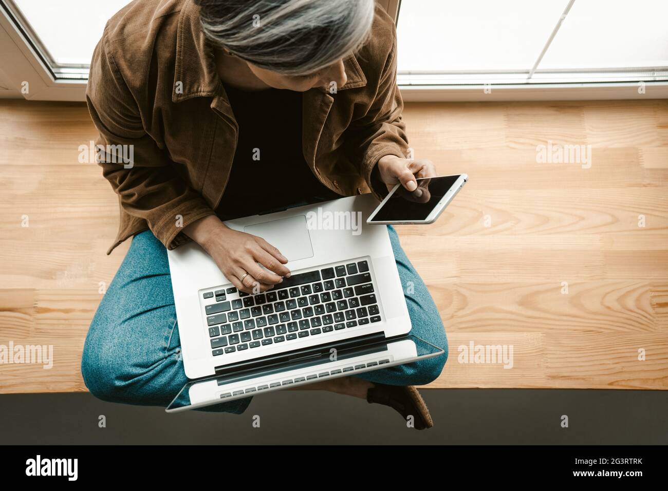 Busy woman looks on mobile screen working laptop computer while sitting ...