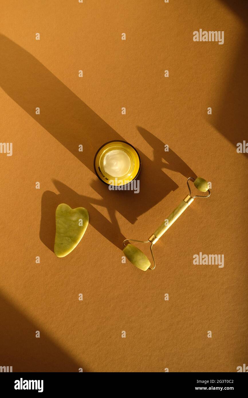 Facial massage roller, gua sha, moisturizer face cream in sunlight ...