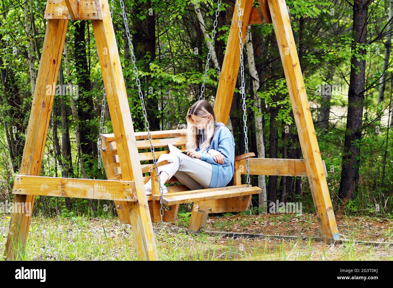 A teenage girl reads a book while sitting on a swing Stock Photo - Alamy