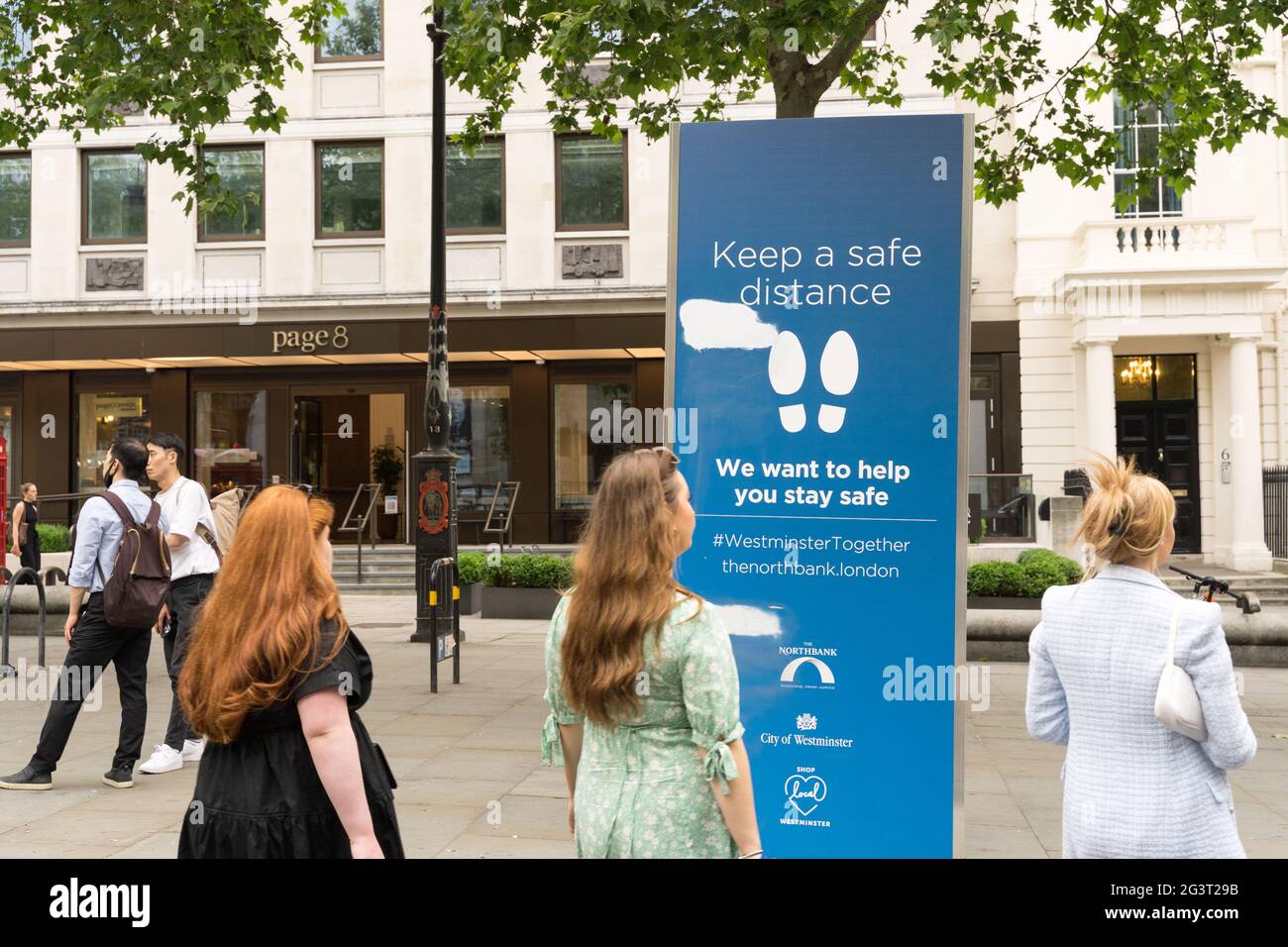poster "keep a safe distance" seen in London street, three women walk ...