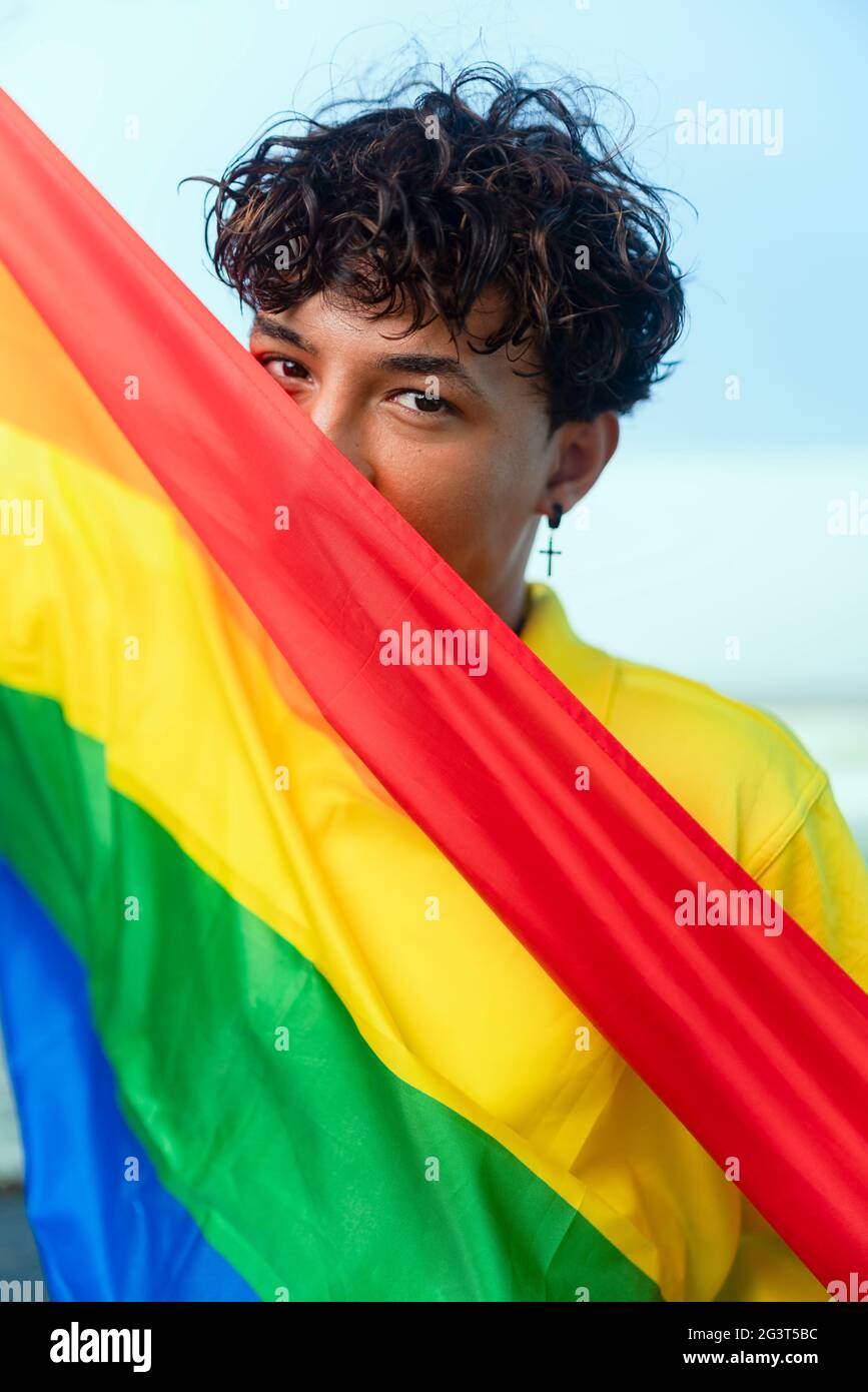 Young gay man covers part of his face with the lgbt flag looking at ...