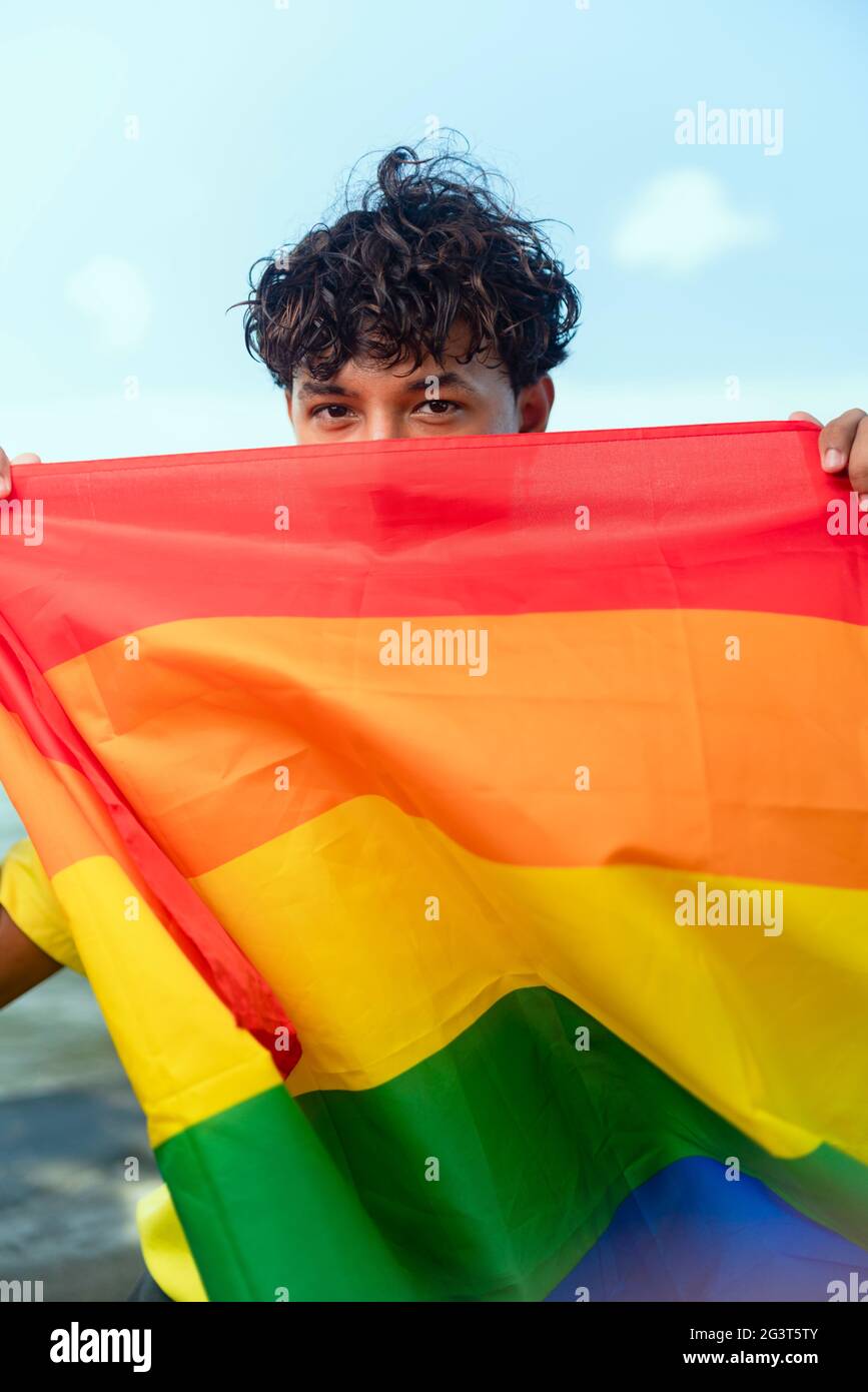 Young gay man covers part of his face with the lgbt flag looking at ...