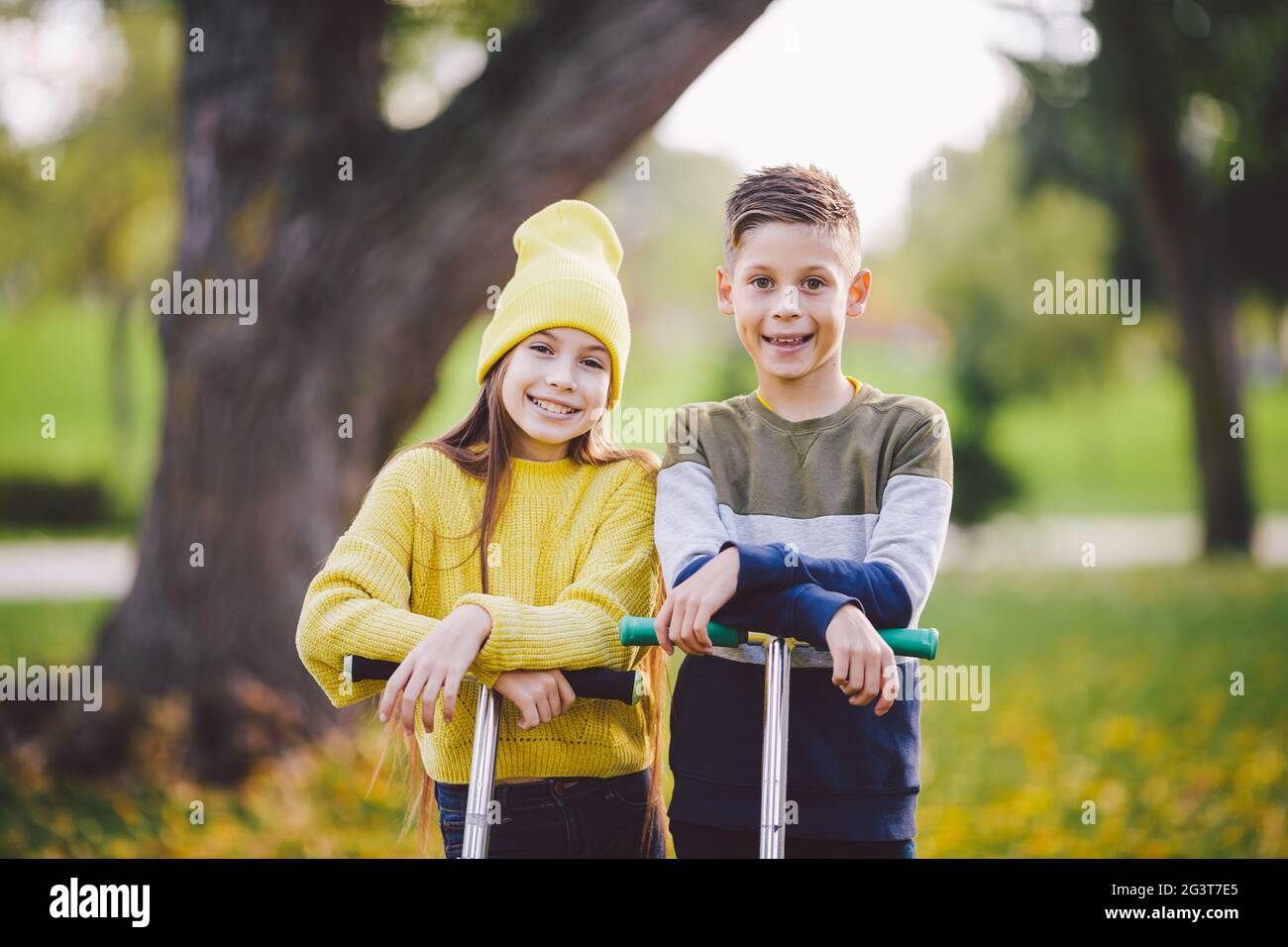 Two children caucasian boy and girl twins posing with scooters in ...