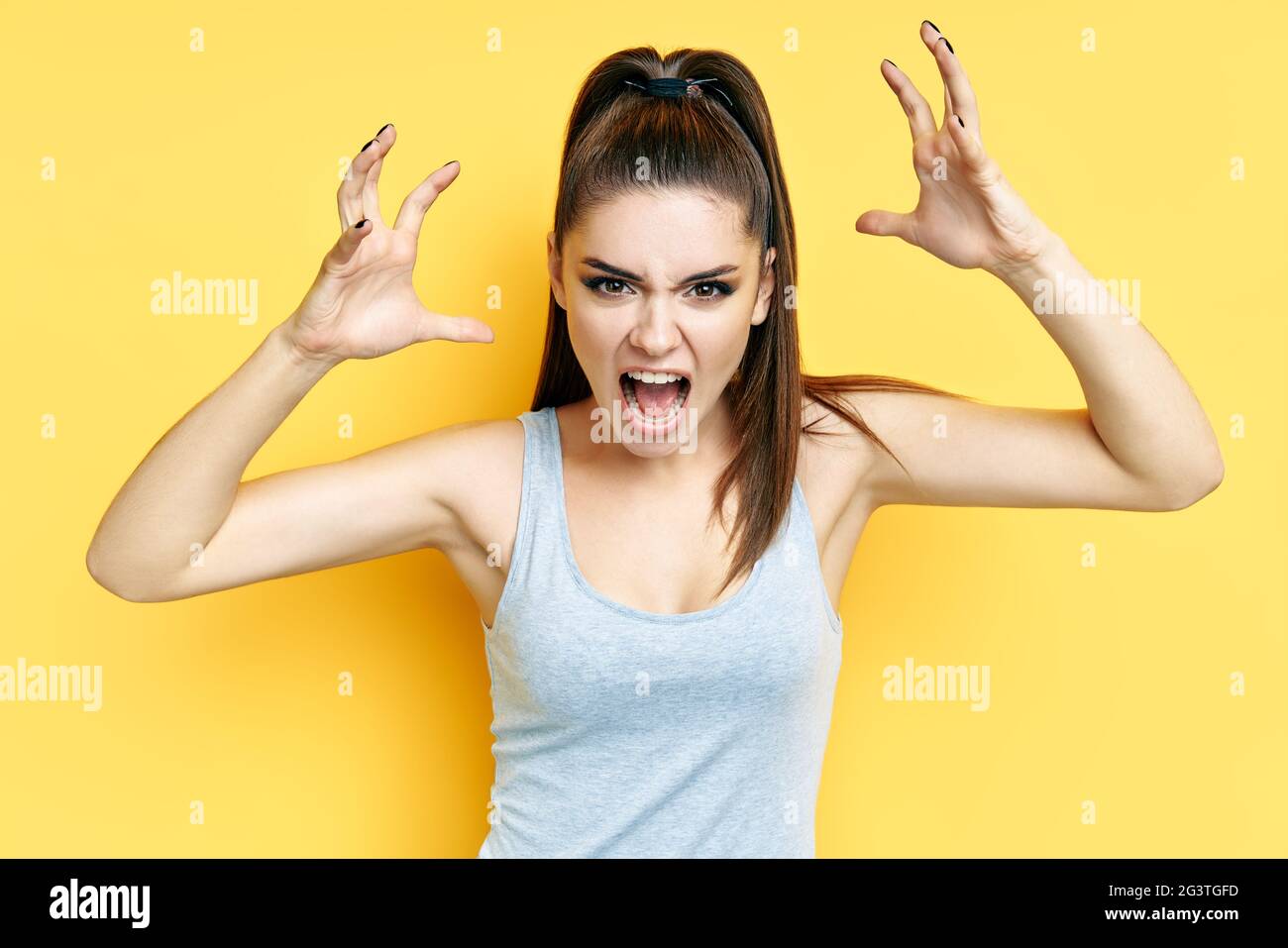 Screaming emotional angry young woman close up portrait over yellow ...