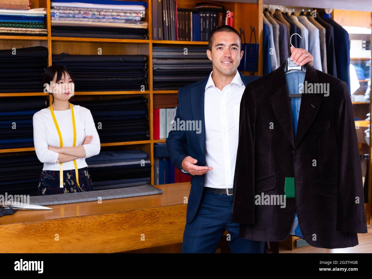 Female seller picks up jacket to man in clothing store Stock Photo - Alamy
