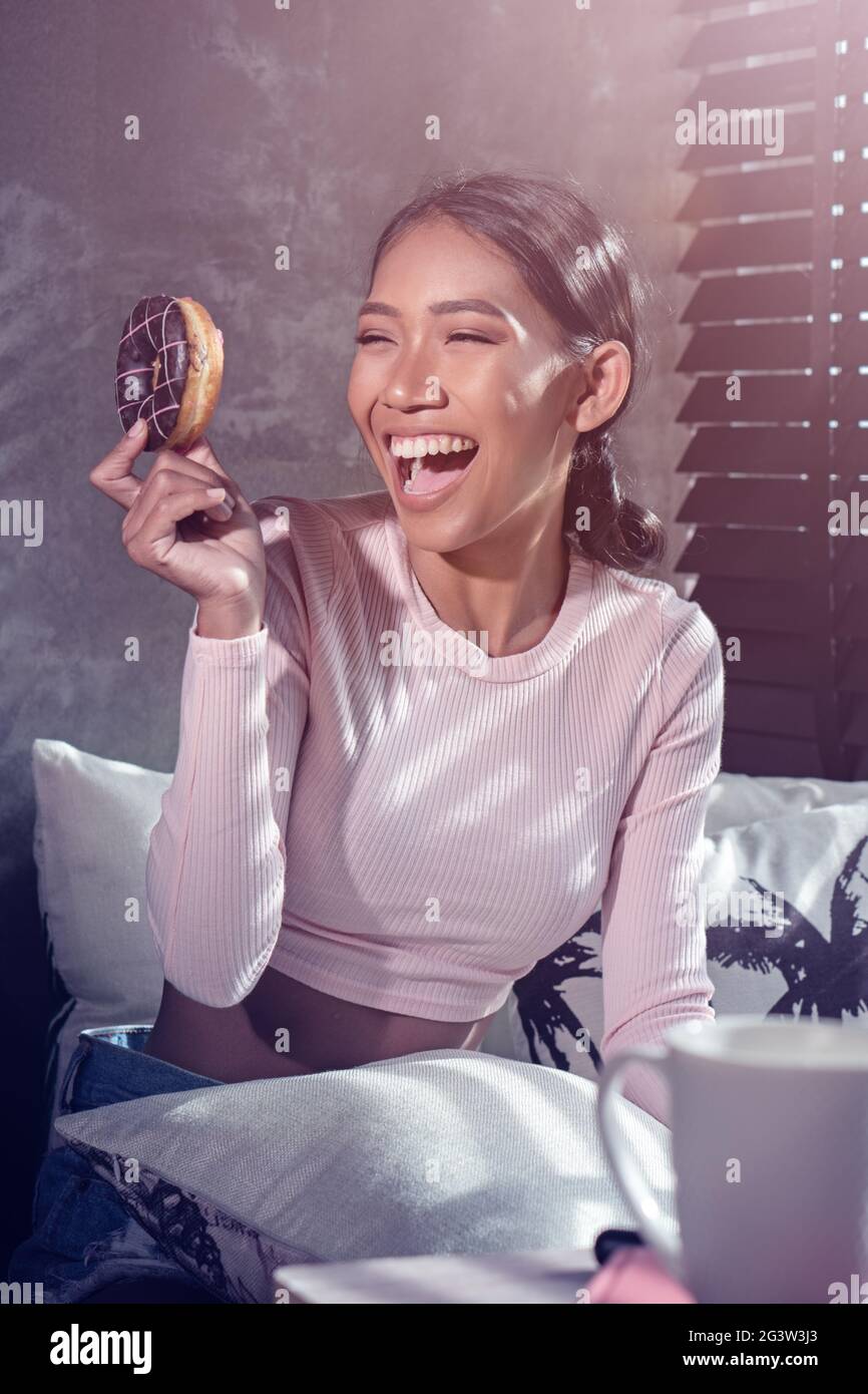 Beautiful smiling girl holding donut and relaxing on her bed at home ...