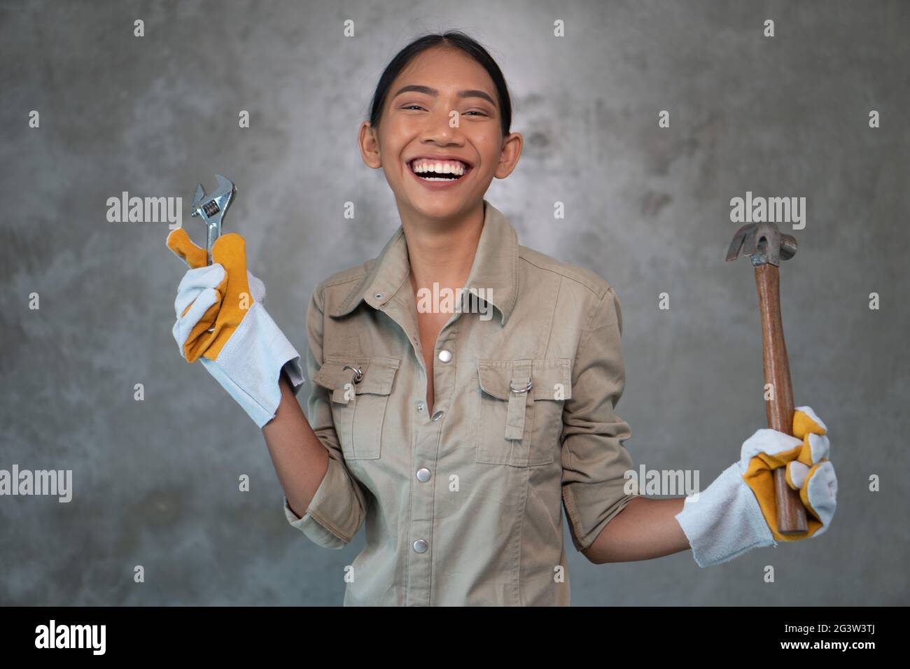 Attractive young girl builder with wrench and hammer over concrete wall ...