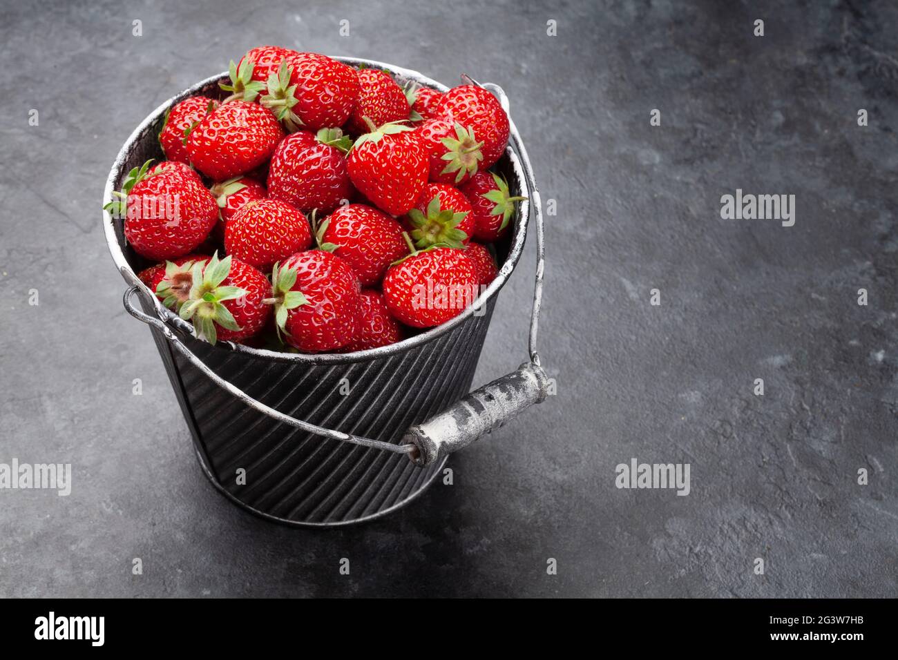 Strawberry bucket with ripe garden berries on stone table. With copy ...
