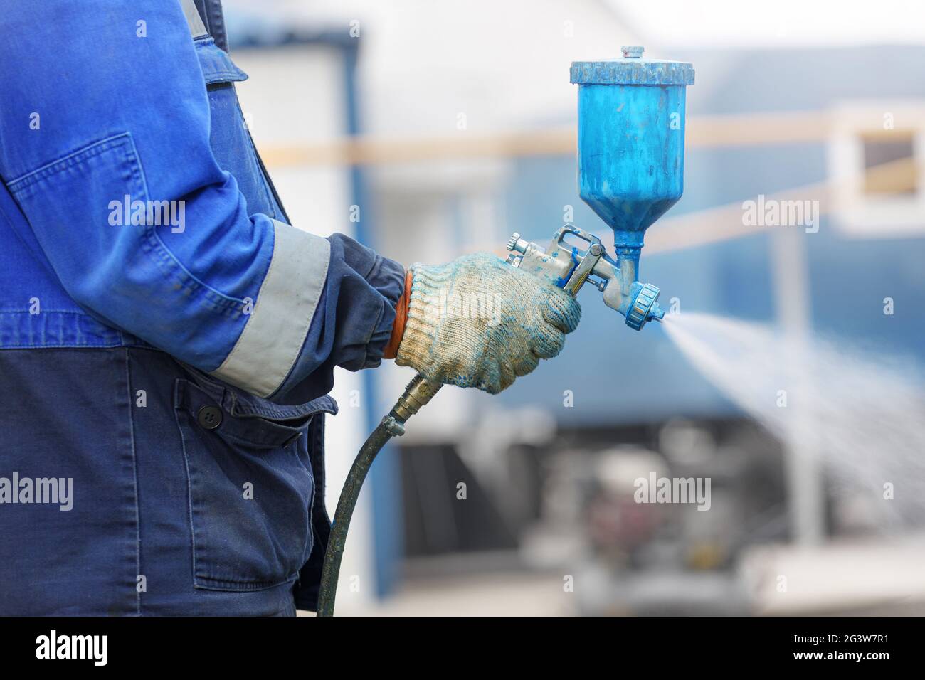 Spray gun in hand. A worker in overalls and a glove holds a spray ...