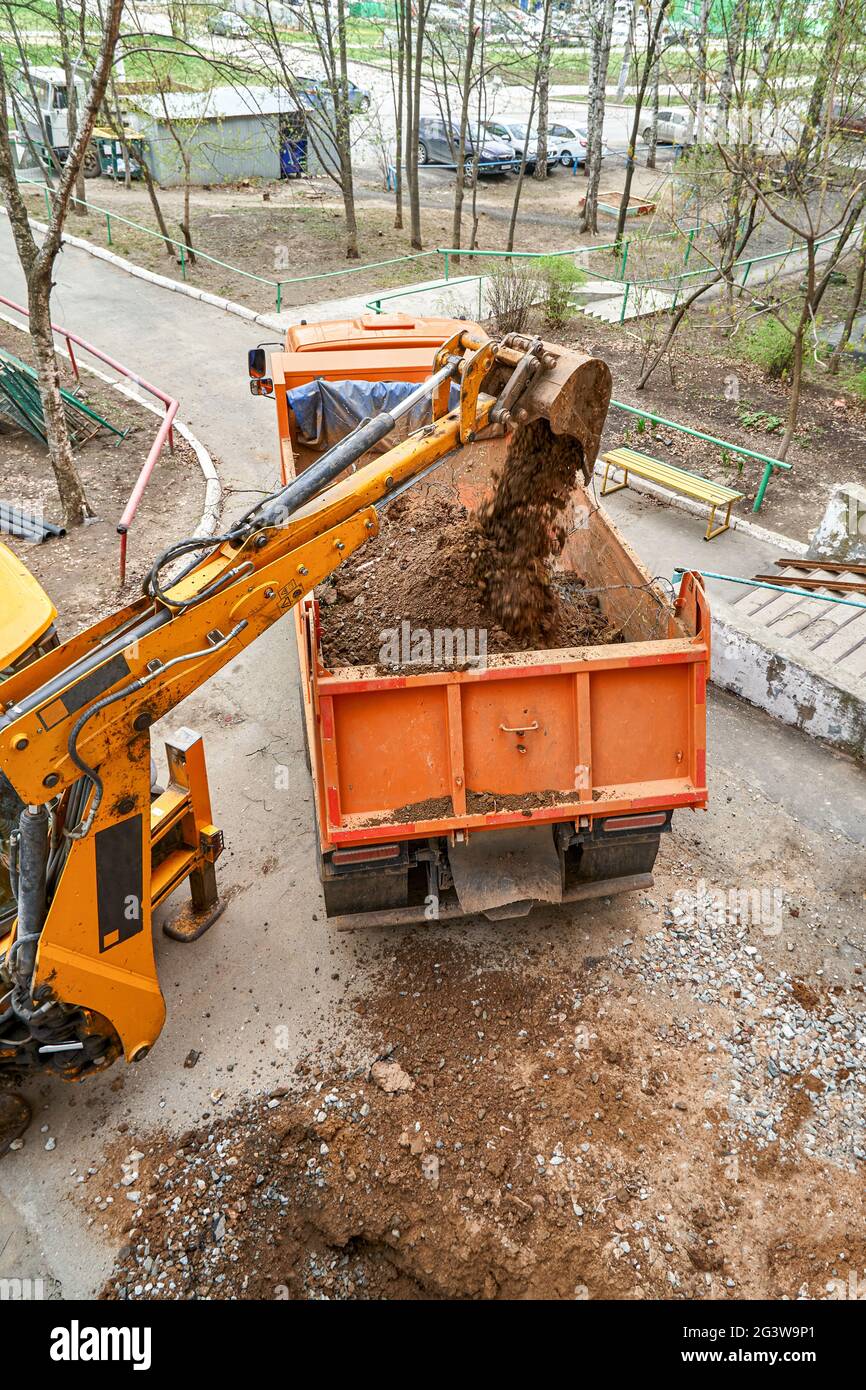 Modern yellow excavator pours dirt into bodywork of tipper truck in ...