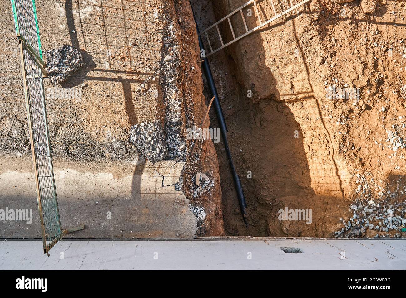 Narrow trench with new water pipeline between green metal fences in ...