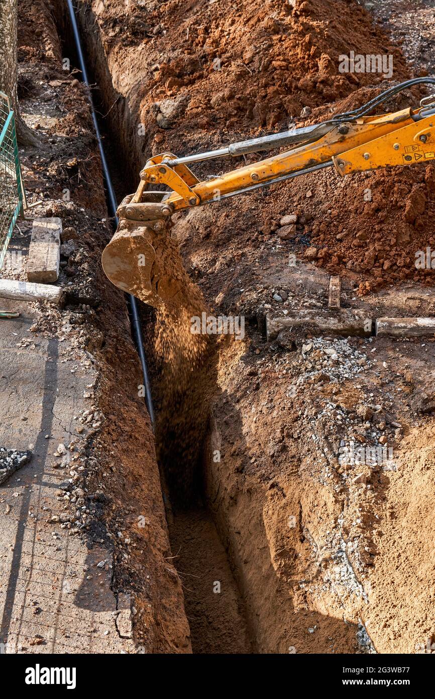 Modern yellow excavator buries narrow trench during changing water ...