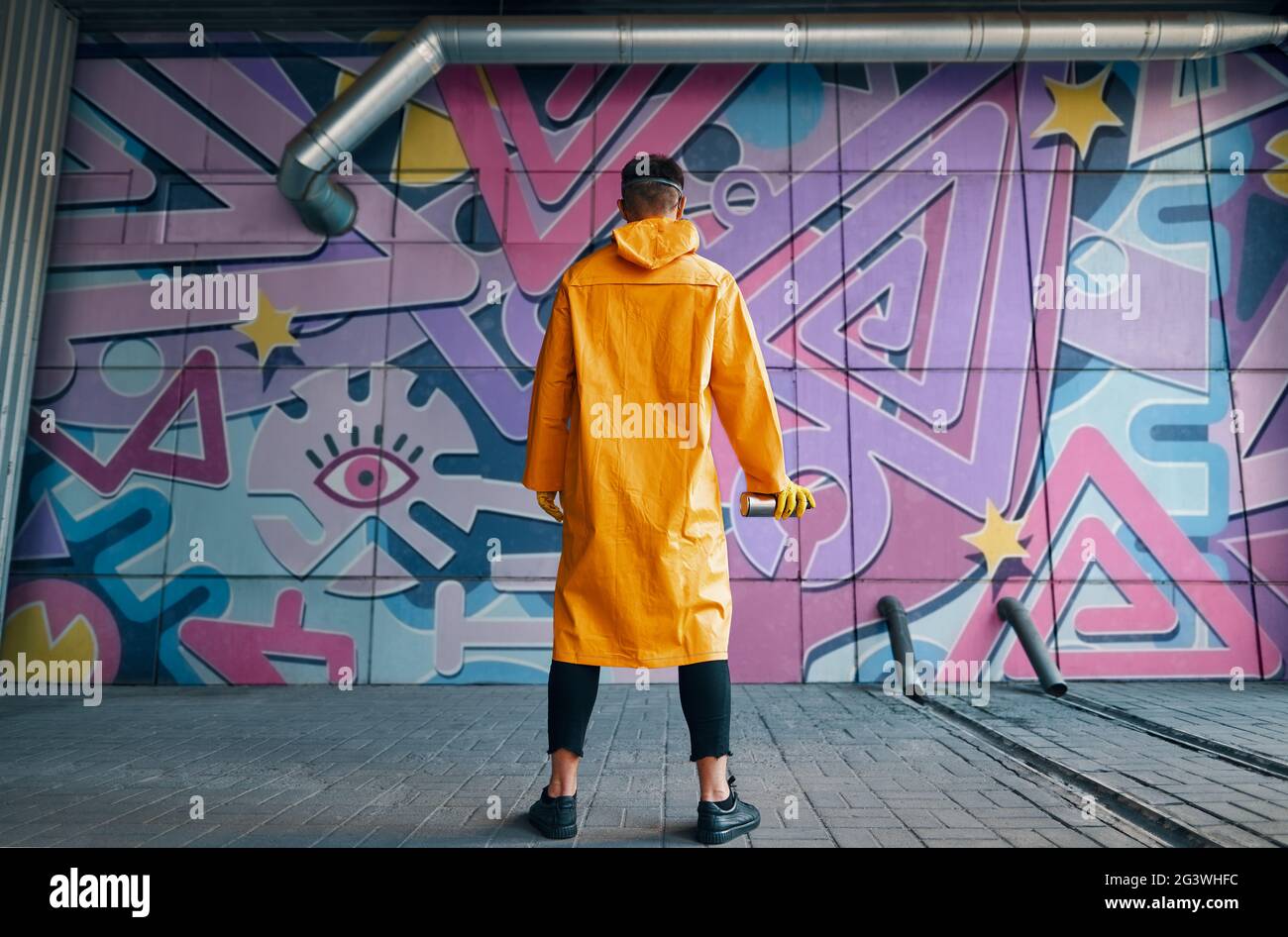 Back view of graffiti painter looking to the wall with his paintings ...