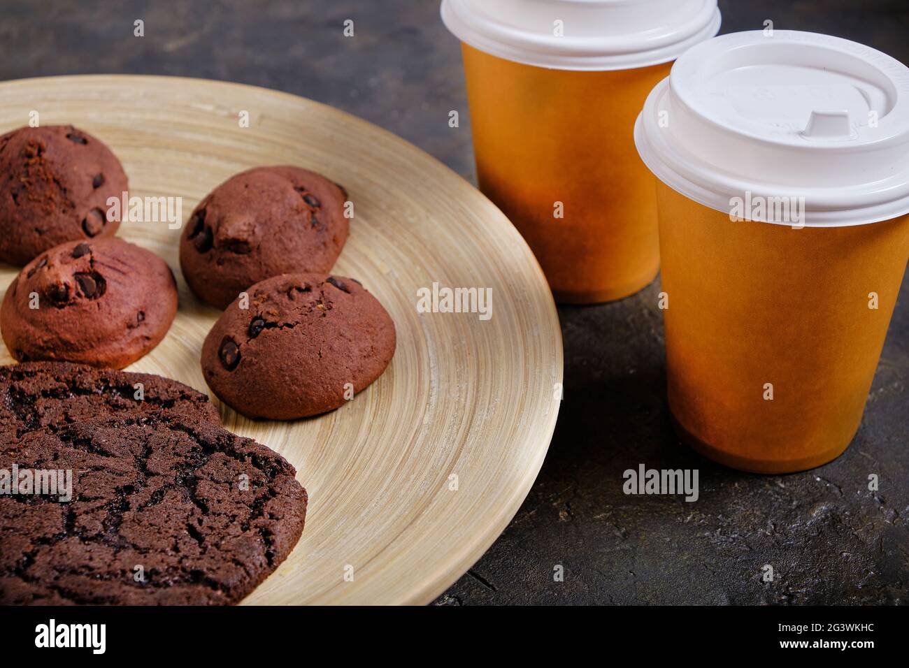 Two glasses takeaway coffee and an American cookie on dark background ...